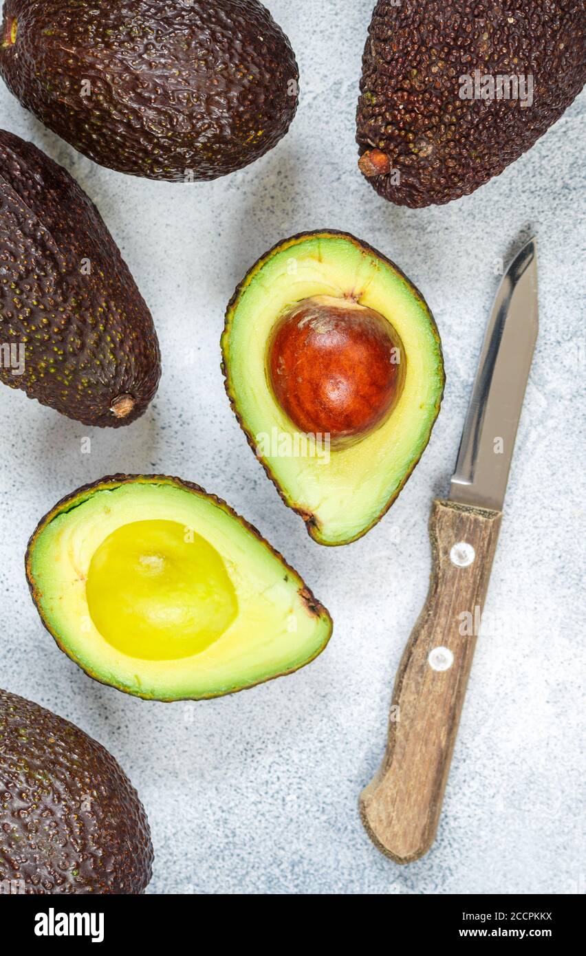 Whole and cut in half ripe organic avocados and a knife on a grey ...