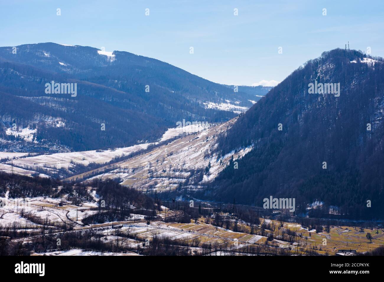 mountainous countryside in early spring. dry grass and leafless trees on the hillside. snow in ...