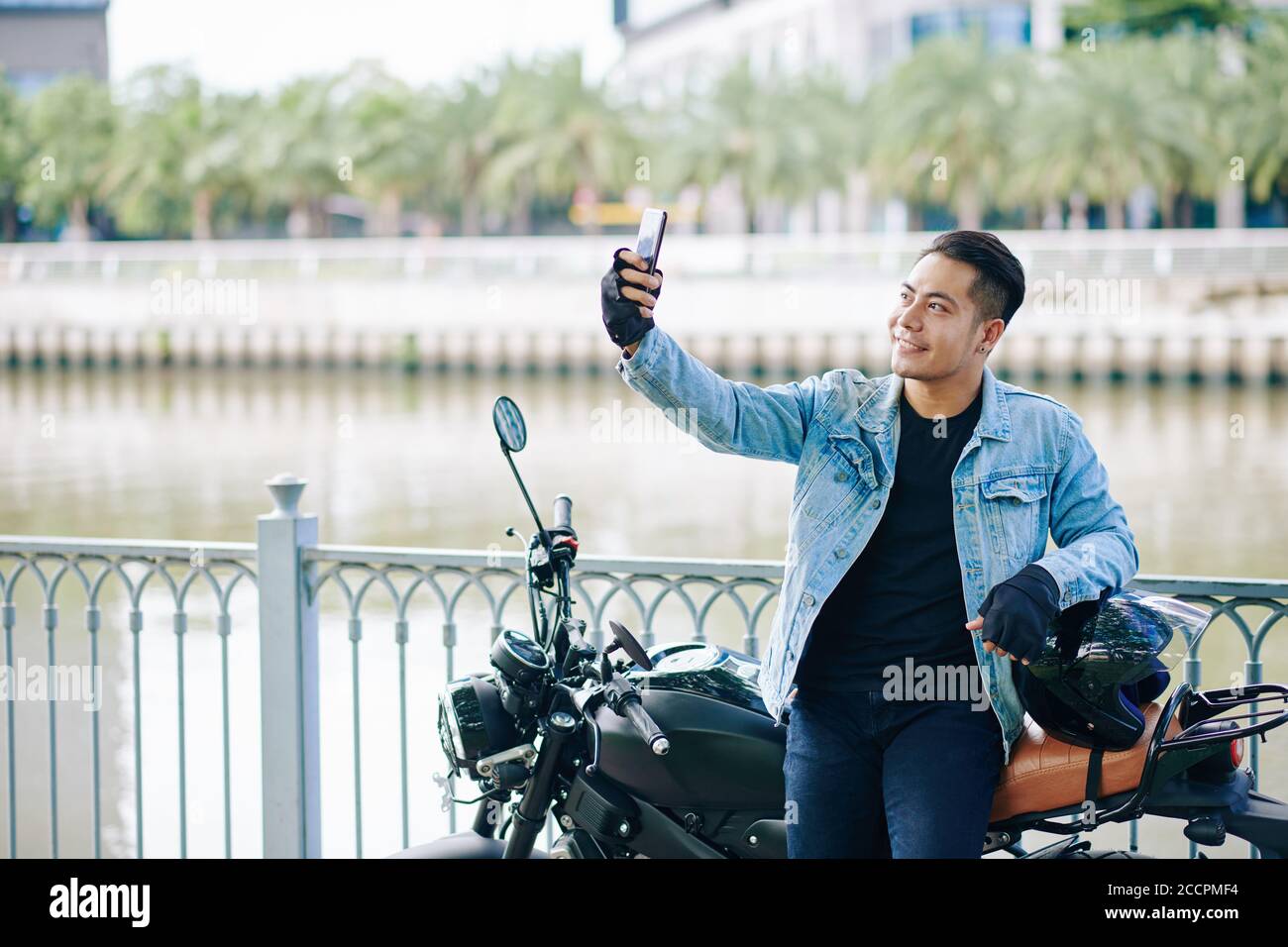 Happy handsome Vietnamese man standing at motorcycle, taking off helmet ...