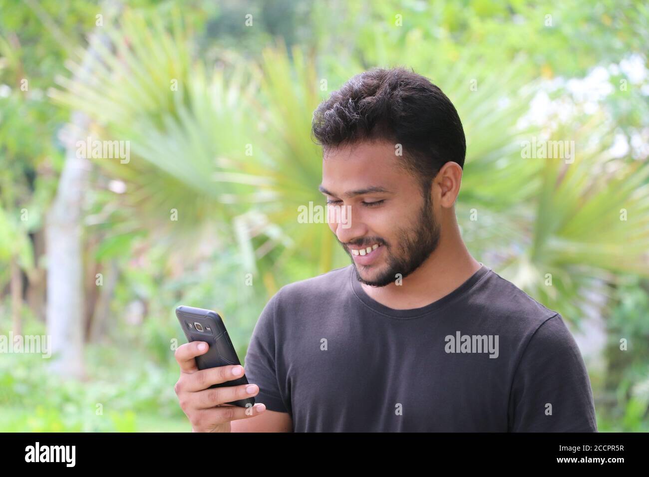 Smiling young man using smartphone, looking at mobile phone screen and ...