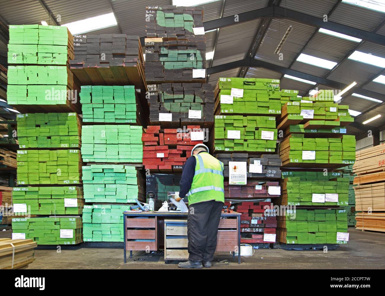A worker checks paperwork in a UK timber warehouse. Bundles or timber ...