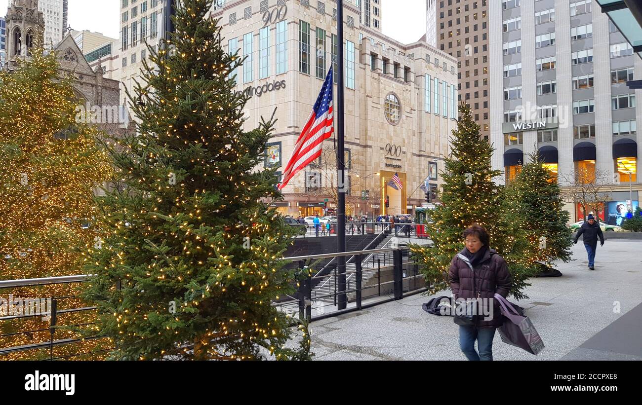 A city shopper walks past Christmas trees and an American flag, Chicago ...