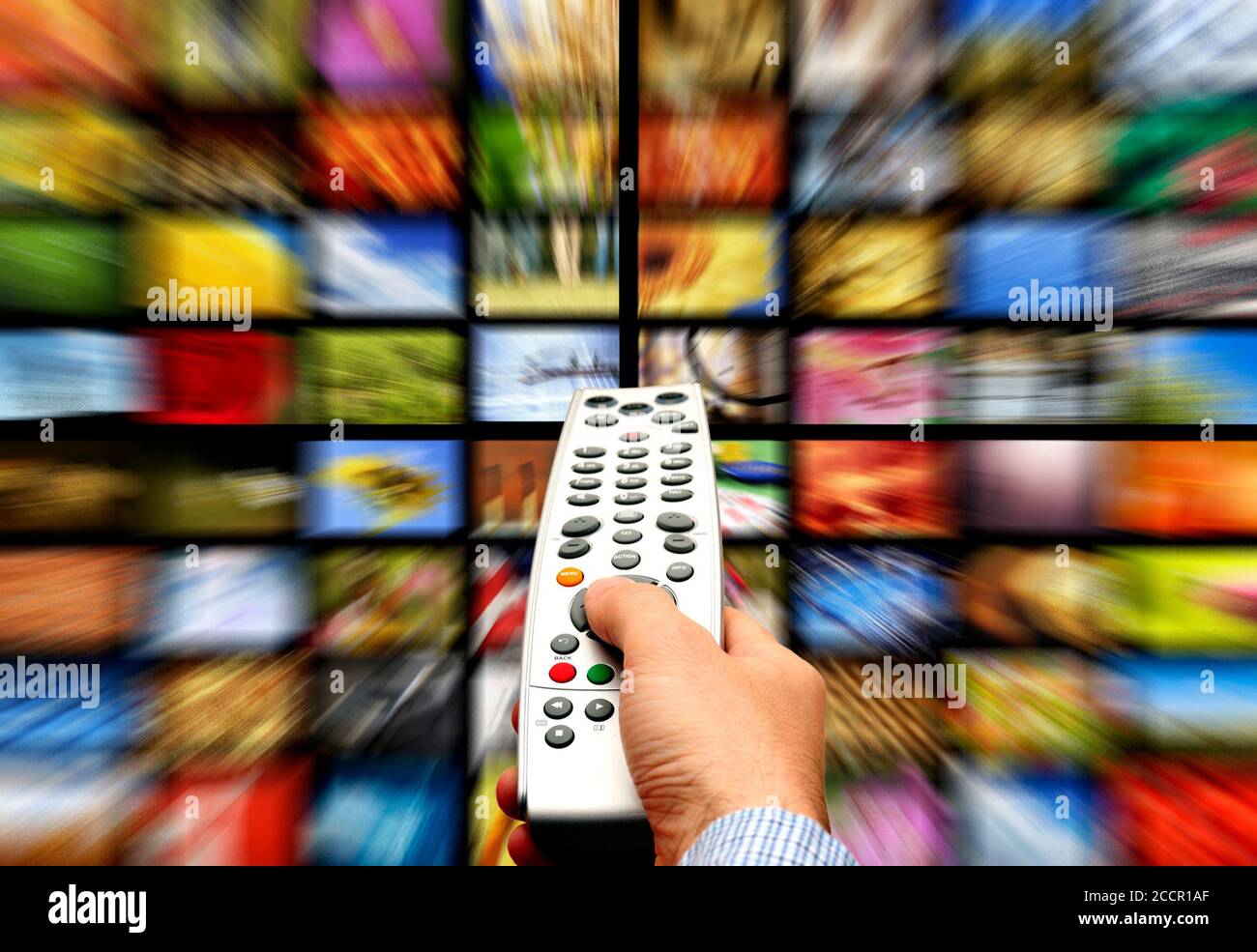 hand holding a remote and many flat panels screens with images, as ...