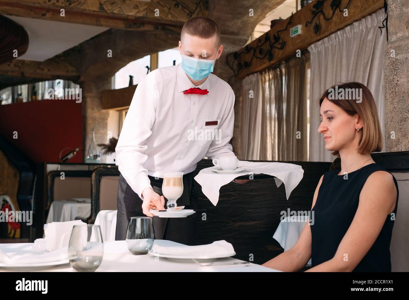 A European-looking waiter in a medical mask serves Latte coffee Stock ...