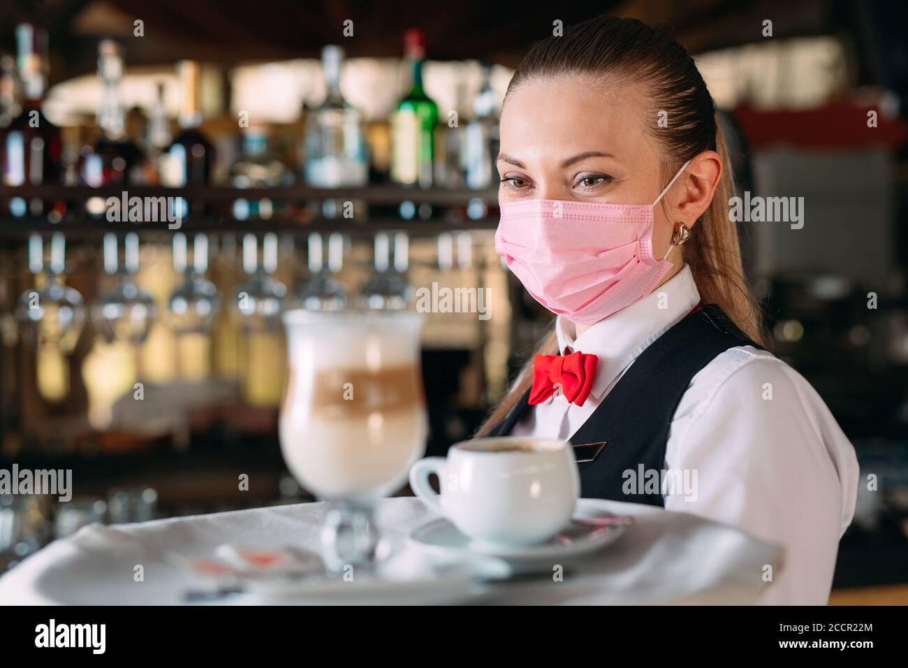 A female Waiter of European appearance in a medical mask serves Latte ...