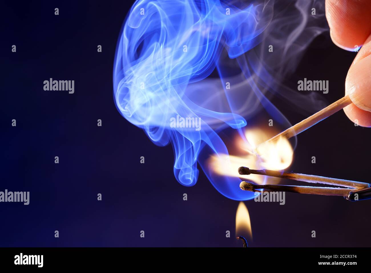 Hand and burning matchsticks with smoke spreading on blue background ...