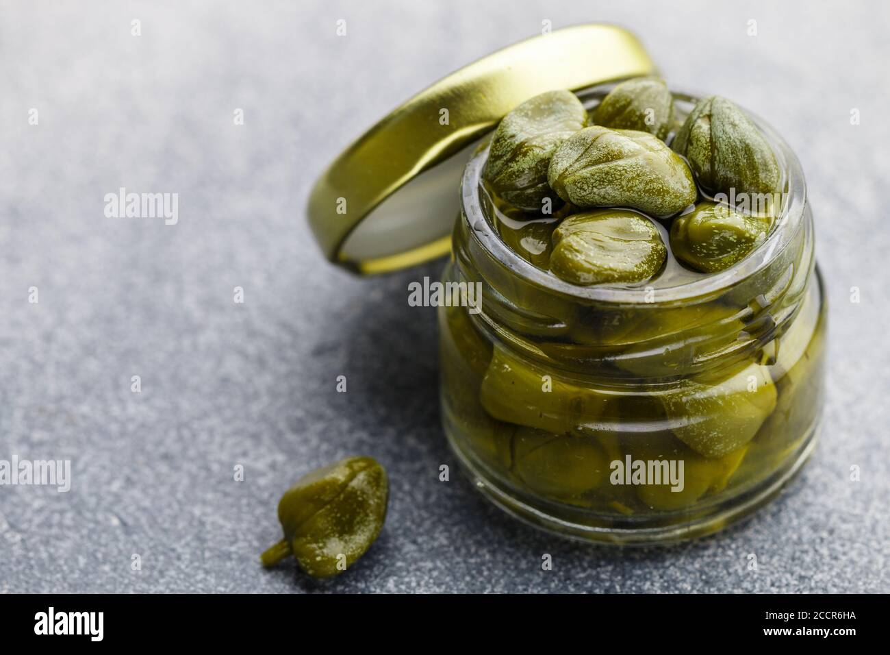Pickled or salted capers in a glass jar close-up. Unopened flower buds ...