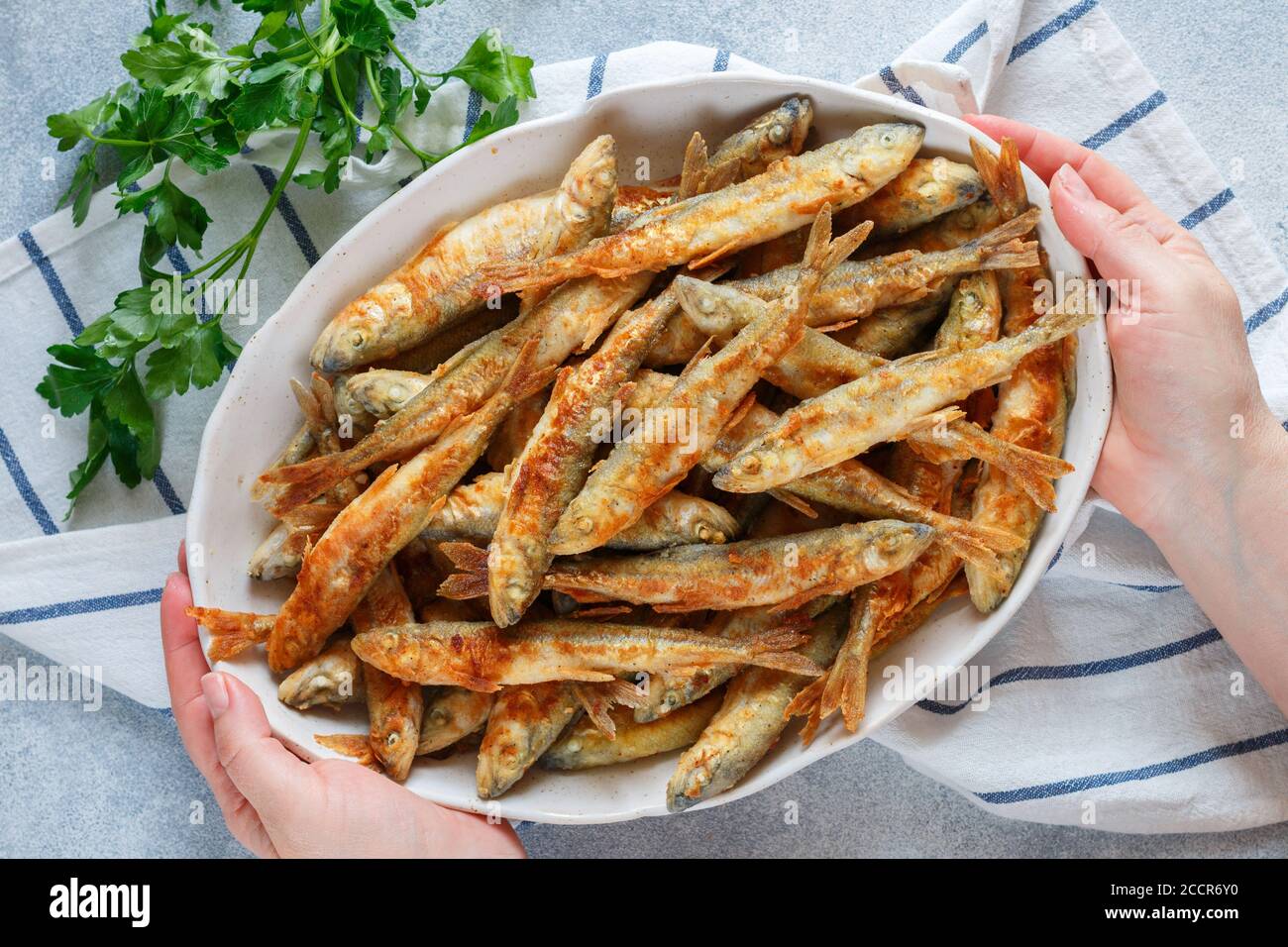 Fried smelt. A woman serves delicious small fish in a white plate ...