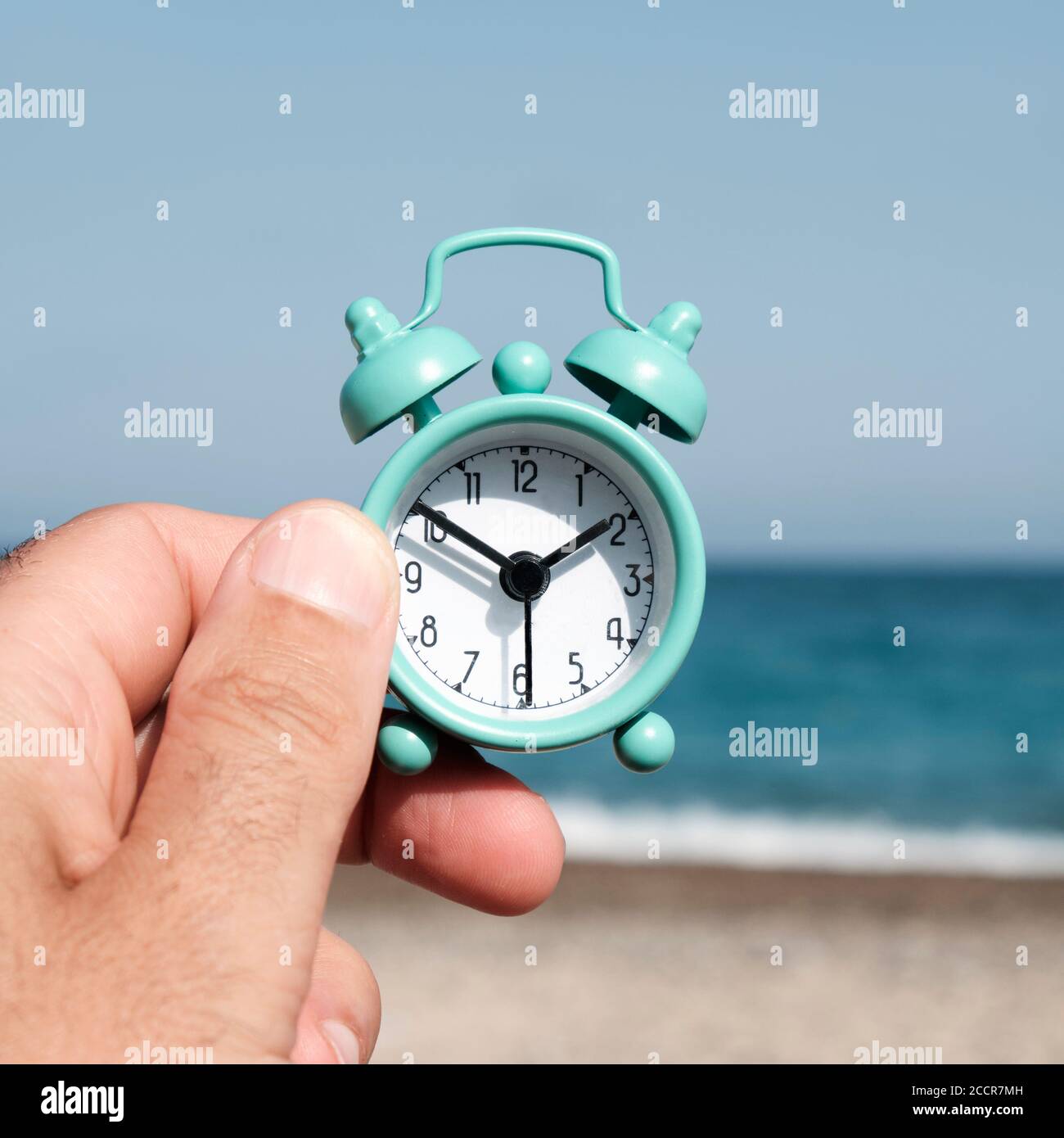 closeup of a caucasian man holding a small pastel green alarm clock in ...