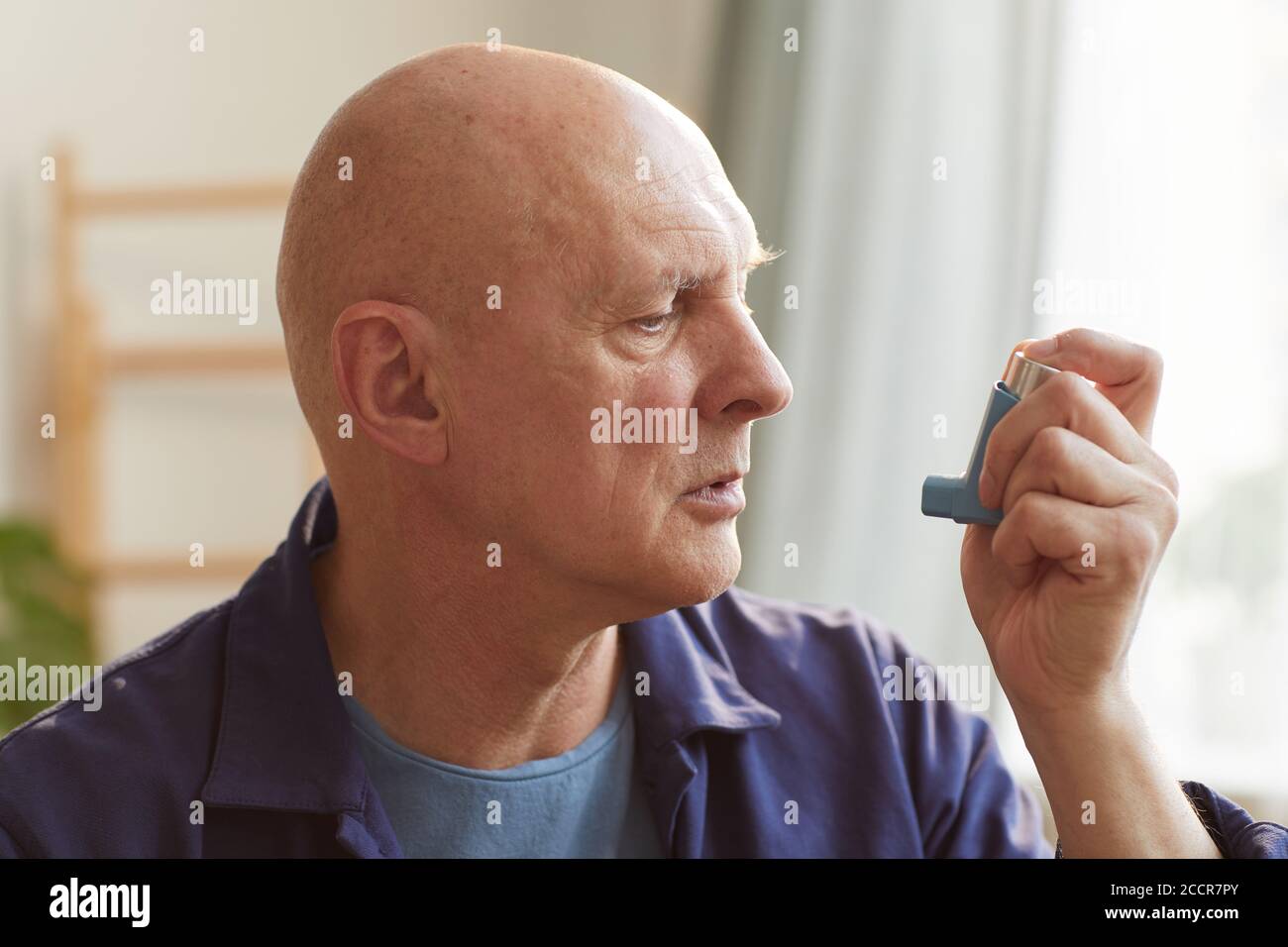 Warm-toned side view portrait of bald senior man using inhaler for ...