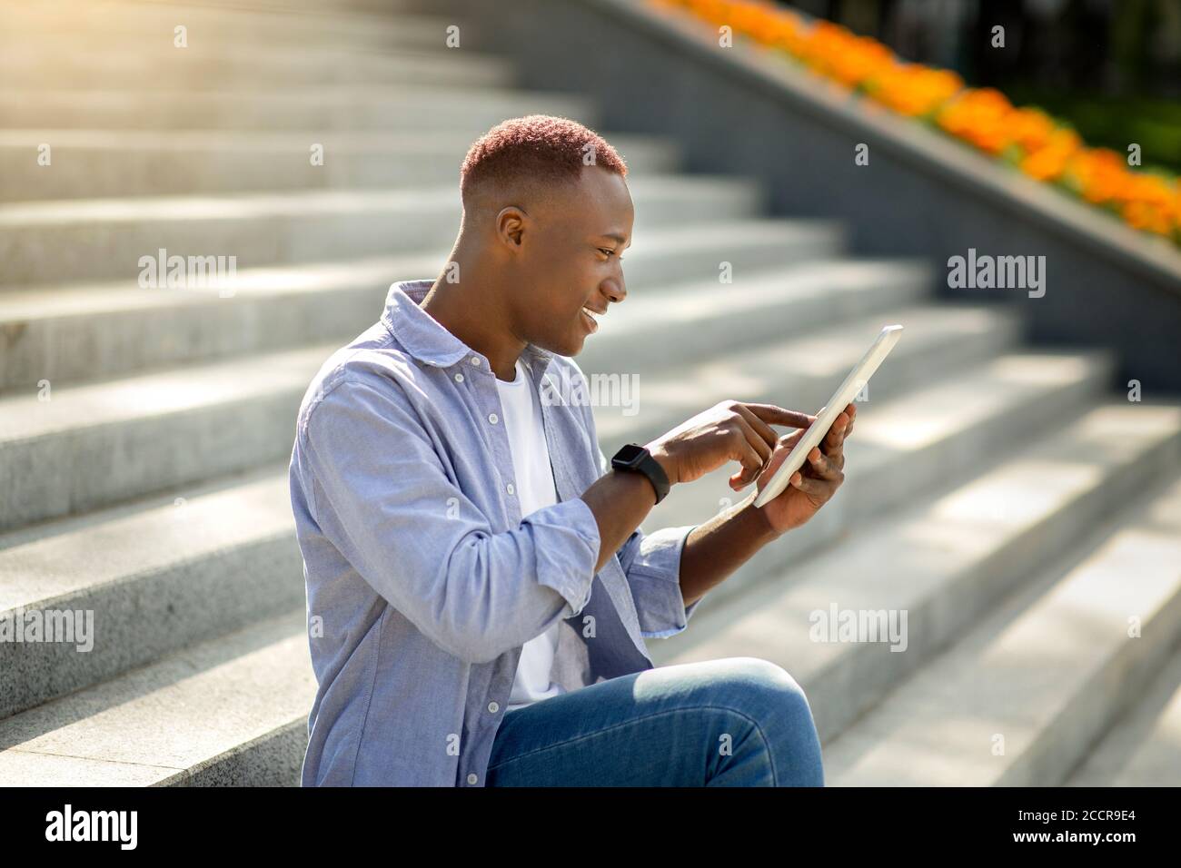 Millennial black man browsing internet on tablet computer while sitting ... Millennial black man browsing internet on tablet computer while sitting ...