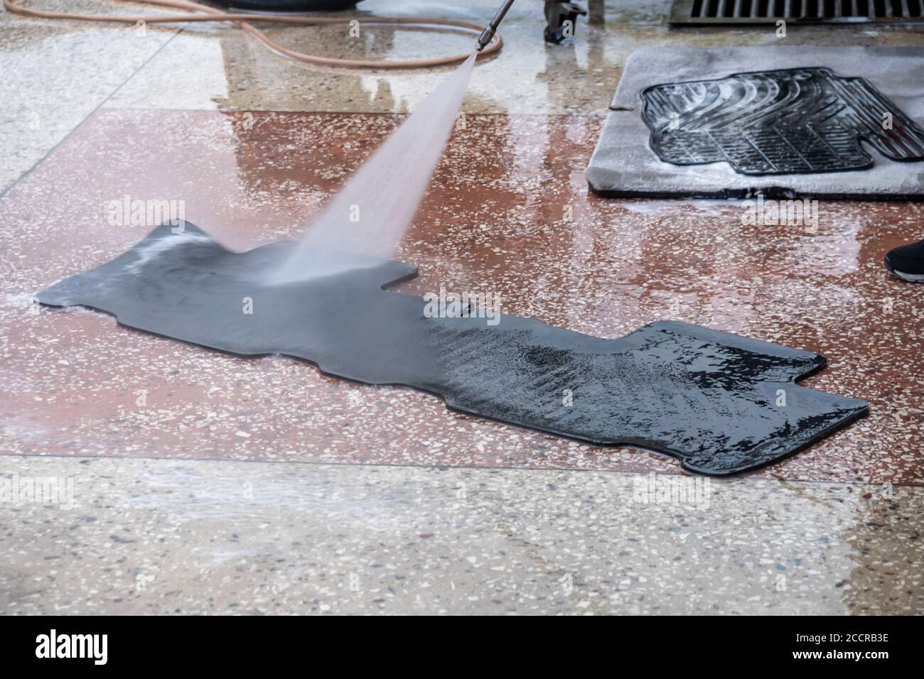 A man washes a black car mat with a strong stream of water Stock Photo ...