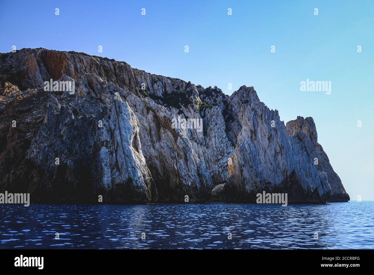 Ocean waves surrounded by the rocky cliffs gleaming under the blue sky ...