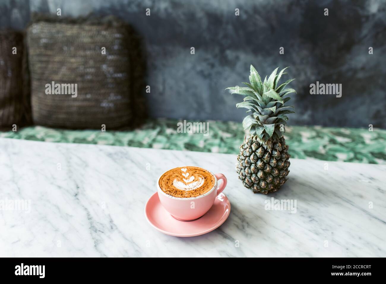 Pink mug of cappuccino and pineapple on marble table in loft cafe with ...