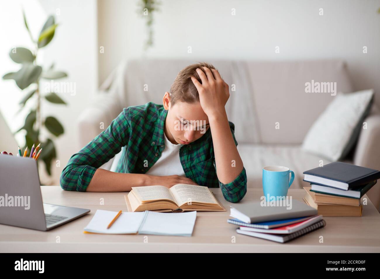 Bored teenager reading book, holding his head Stock Photo - Alamy