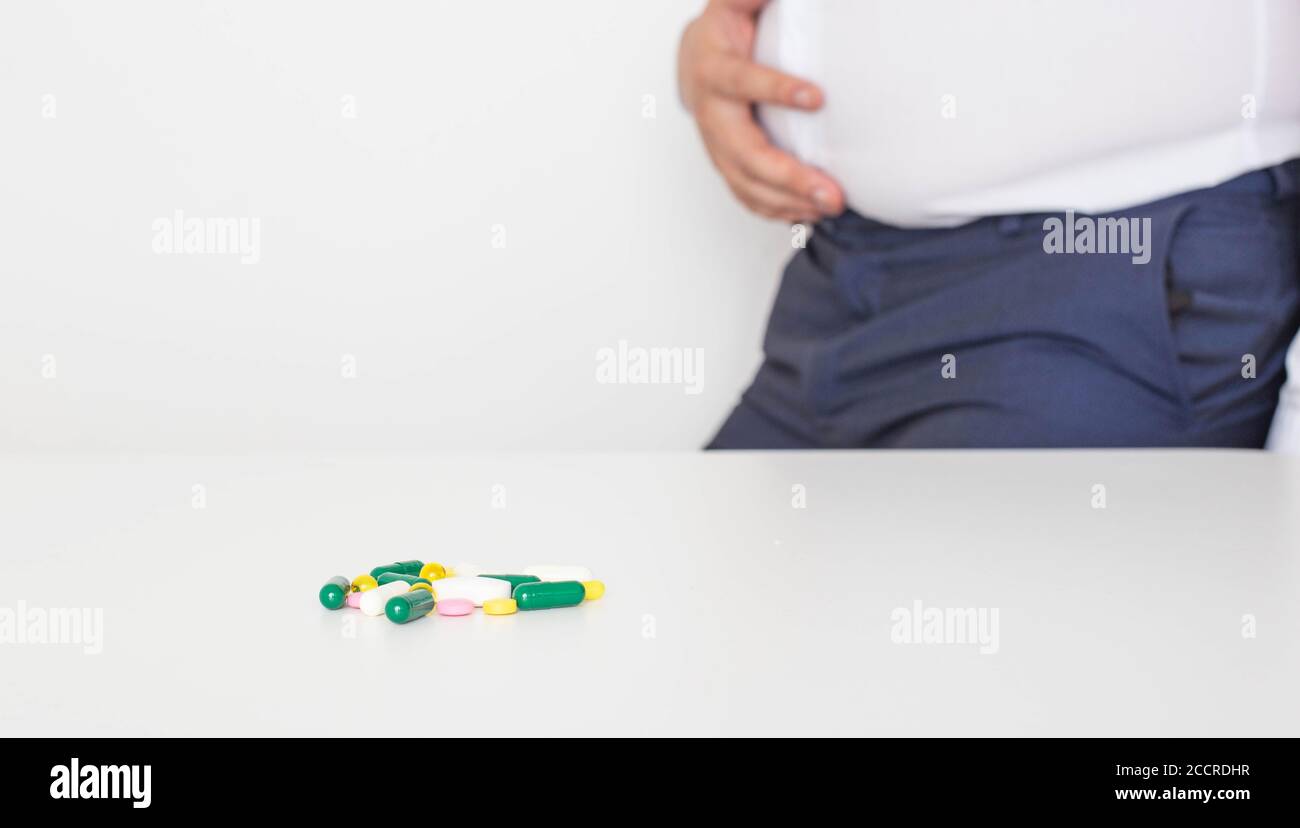 The man is holding onto a fat stomach, in front of him are pills on the ...