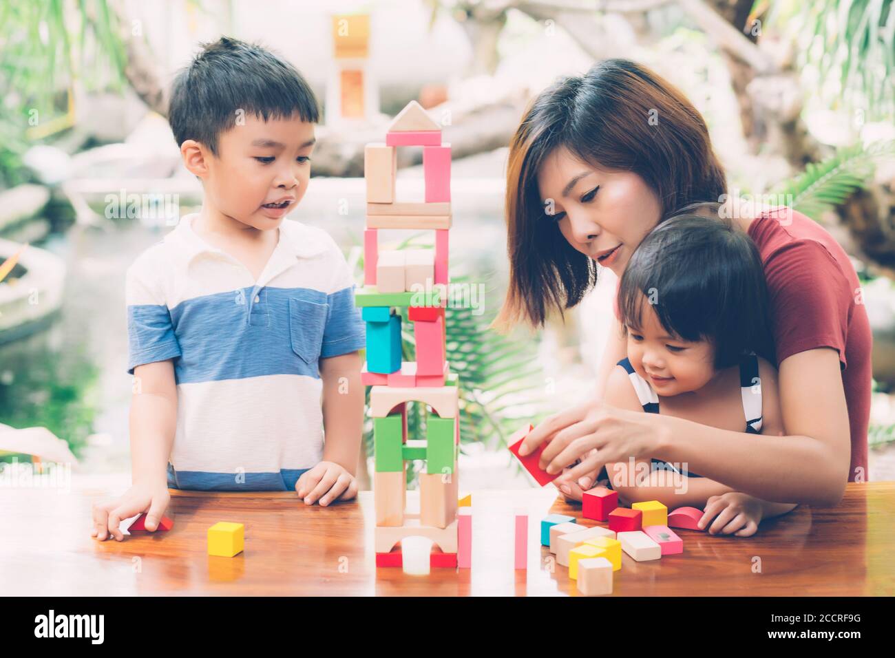 Family with asian mother and children playing toy block at home, mom and son and daughter doing ...