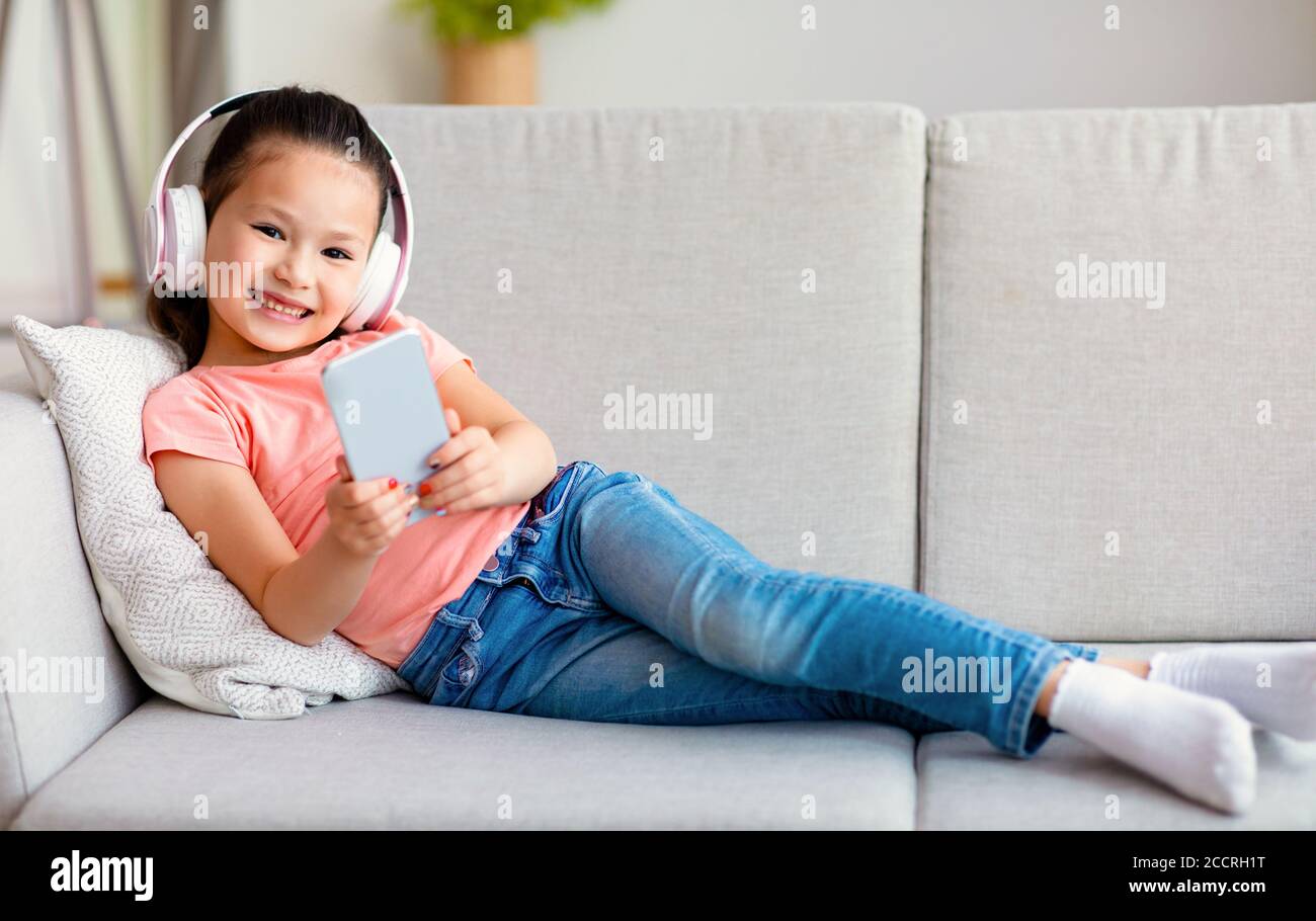 Asian Little Girl In Headphones Using Mobile Phone At Home Stock Photo ...