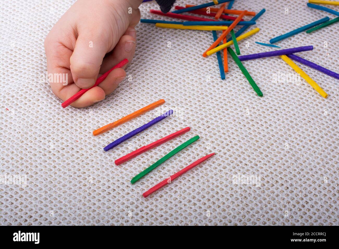 Kid playing with coloured wooden sticks for creativity on white ...