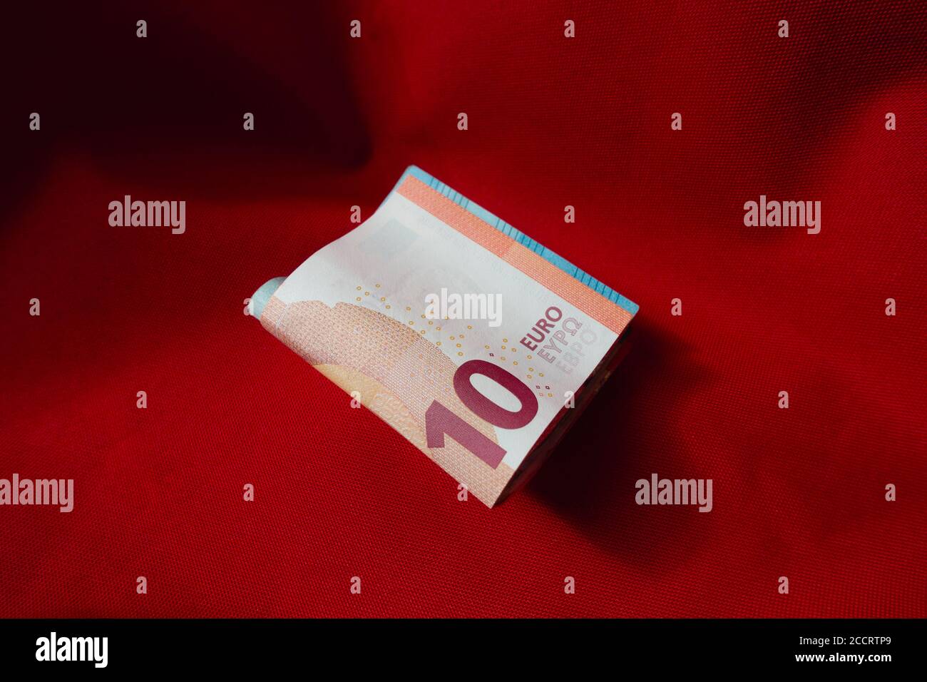 Money bundle with a 10 Euro note on top, lying on a red background ...