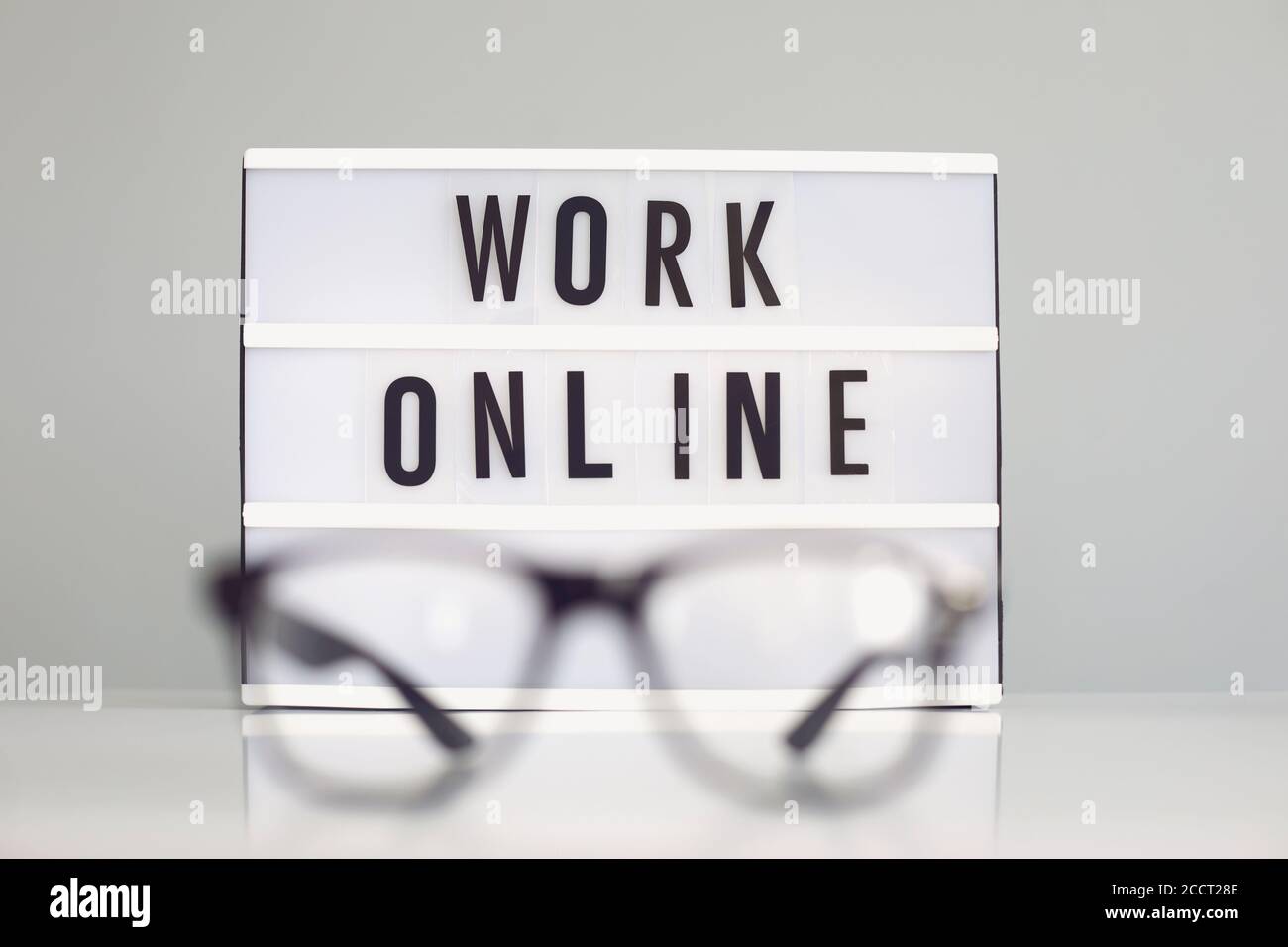 Glasses on desk and blurred sign with words WORK ONLINE against grey ...