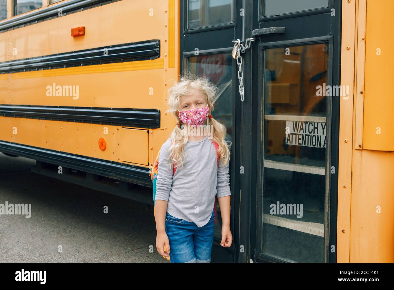 Sad girl student with face mask near locked yellow bus. Closed school ...