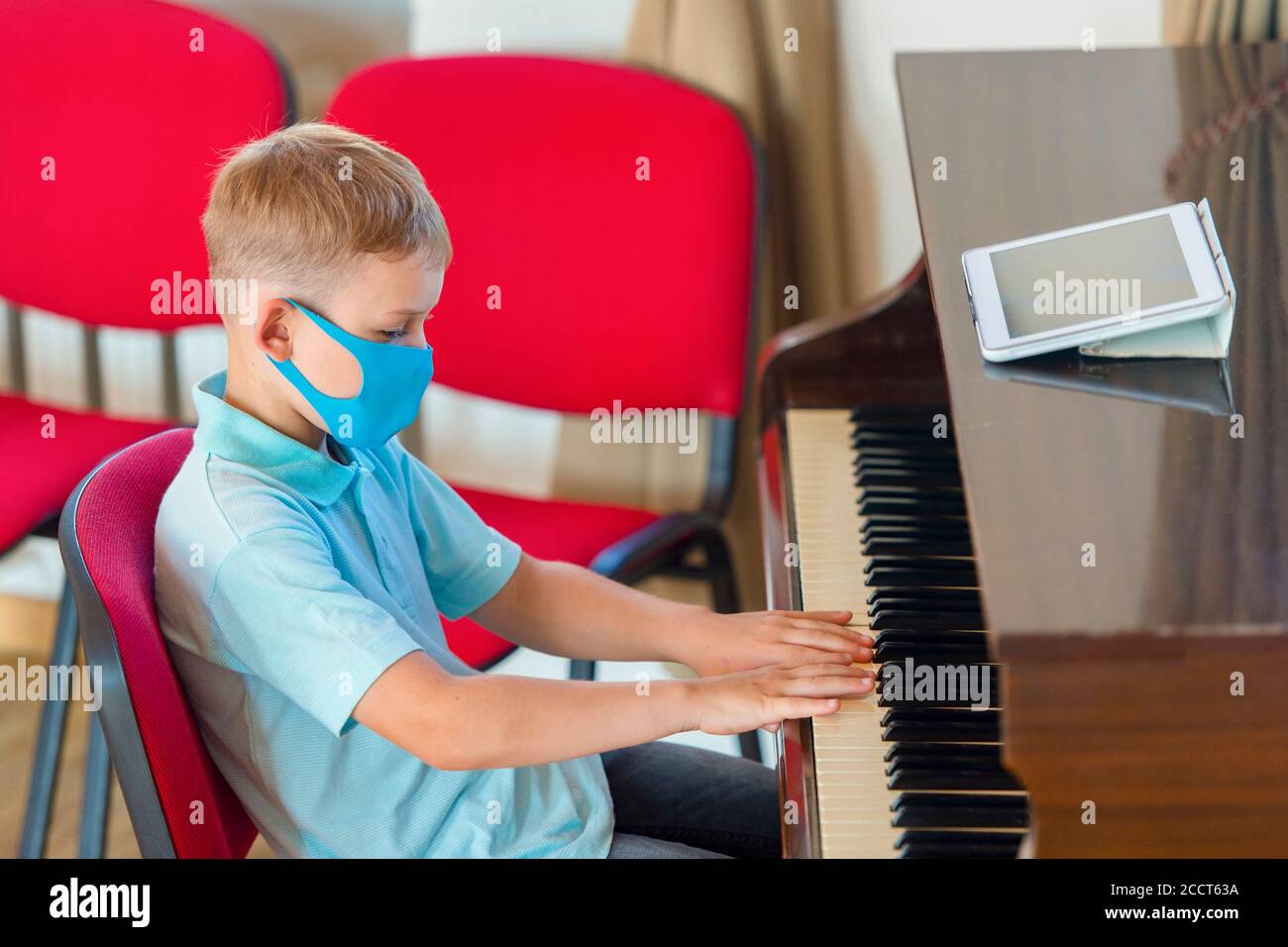 Kid wearing a mask and playing the piano at lesson and event. Kids back ...