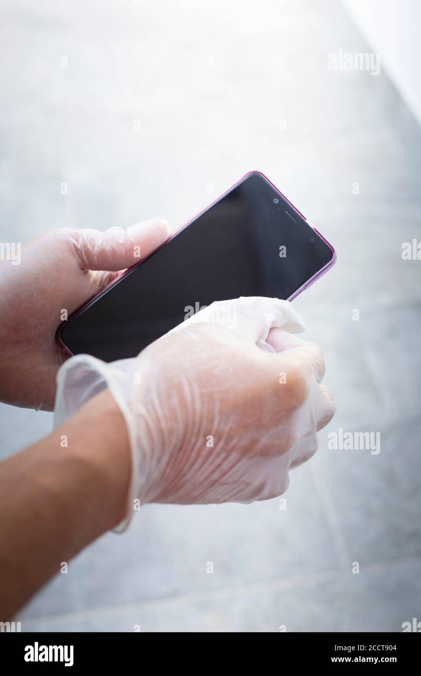 Hands with disposable gloves on, wiping smartphone screen with a white ...