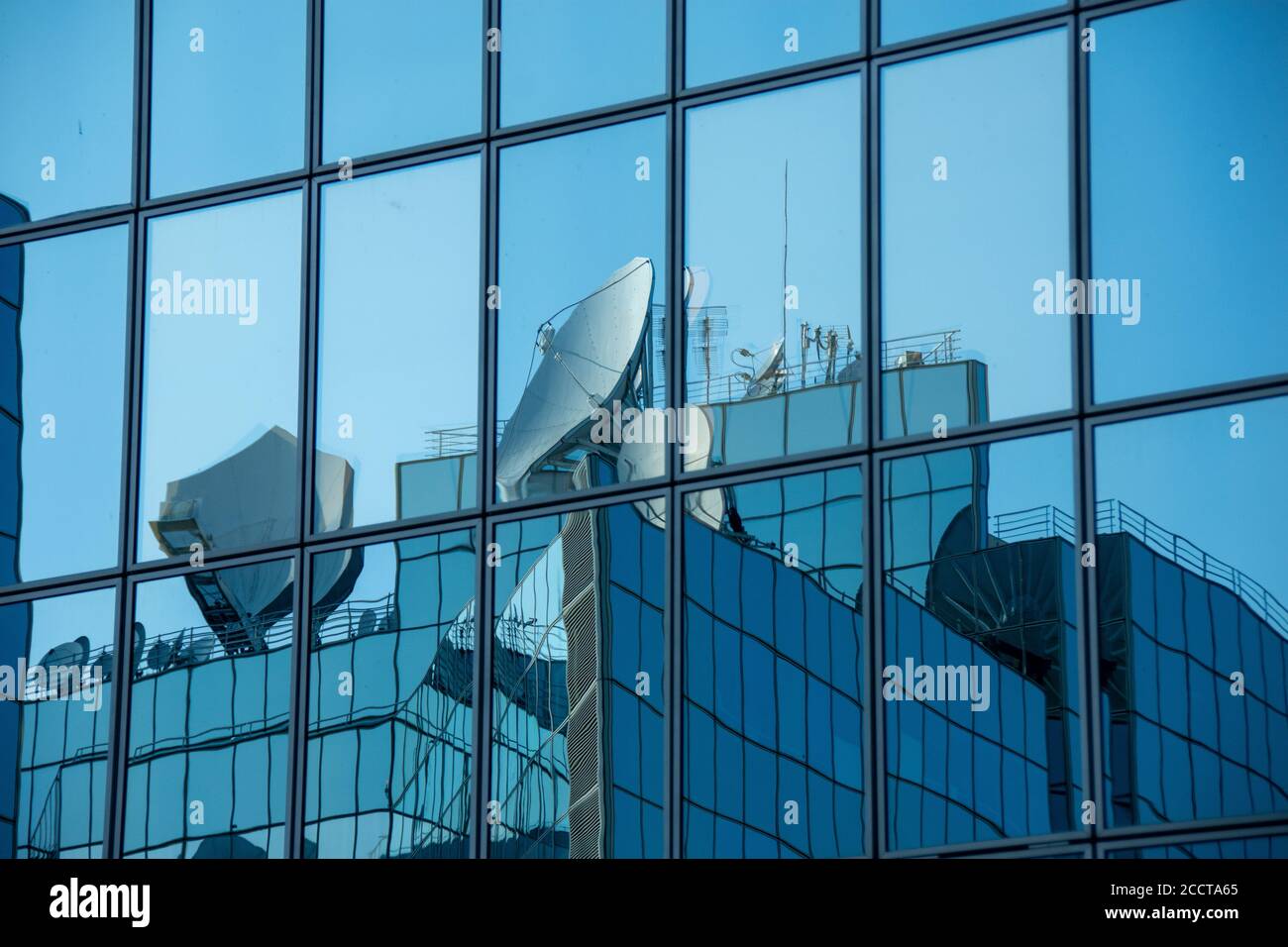 Satellite dishes reflected in the windows of a modern office building ...