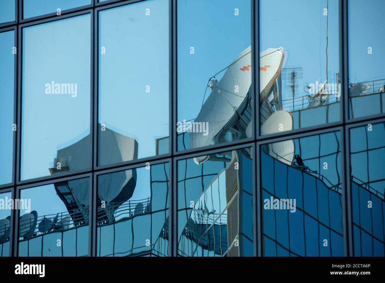 Satellite dishes reflected in the windows of a modern office building ...