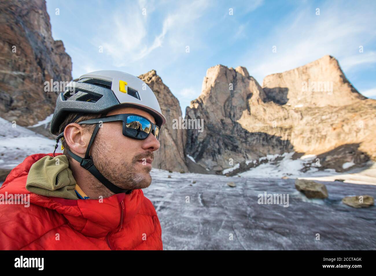 Portrait of climber wearing helmet and sunglasses below mountain summi ...