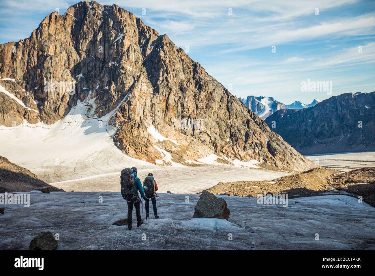 Two backpackers cross a glacier below mountain range Stock Photo - Alamy