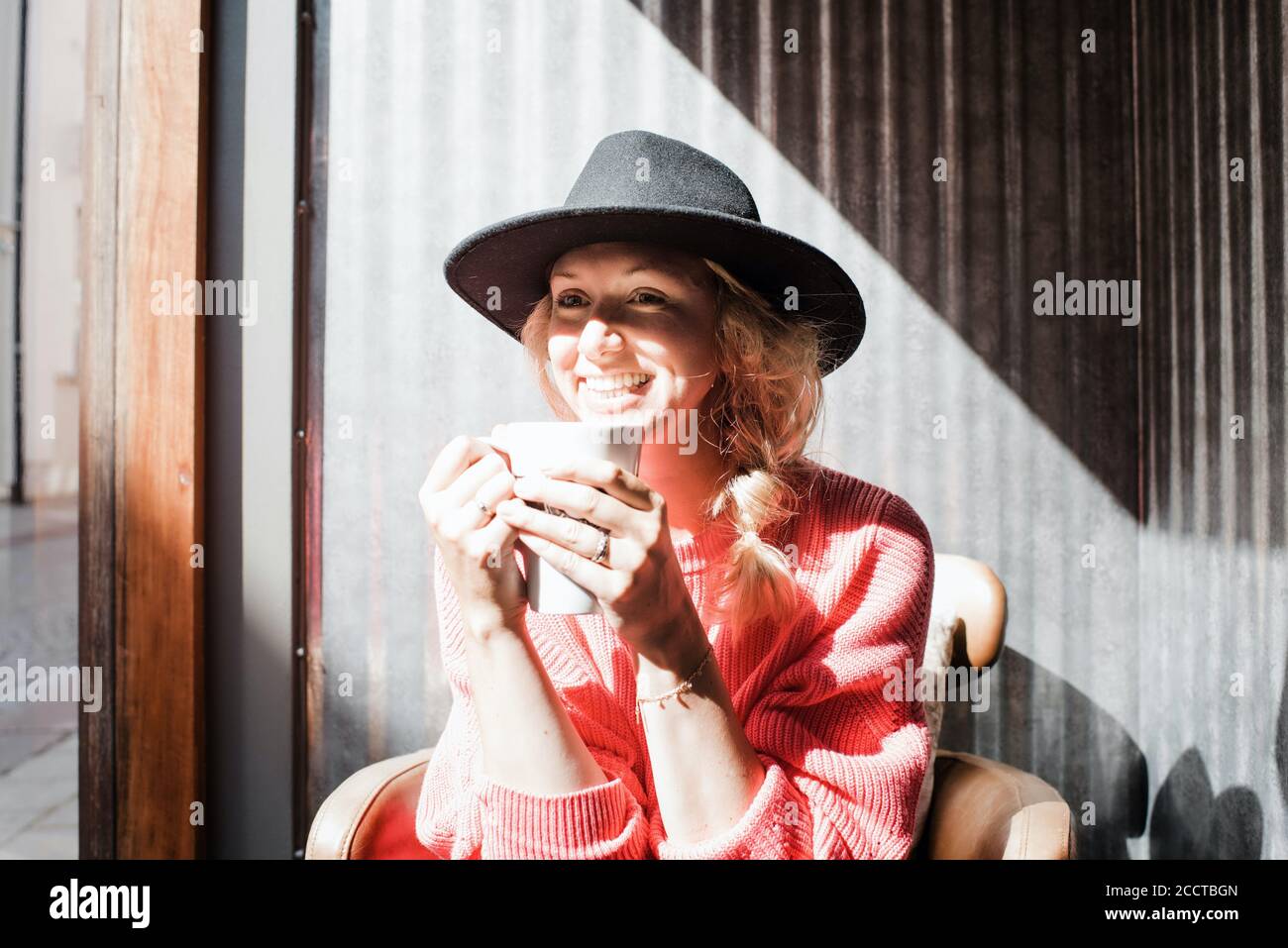 woman smiling whilst drinking coffee in the sunshine in a cafe in fall ...
