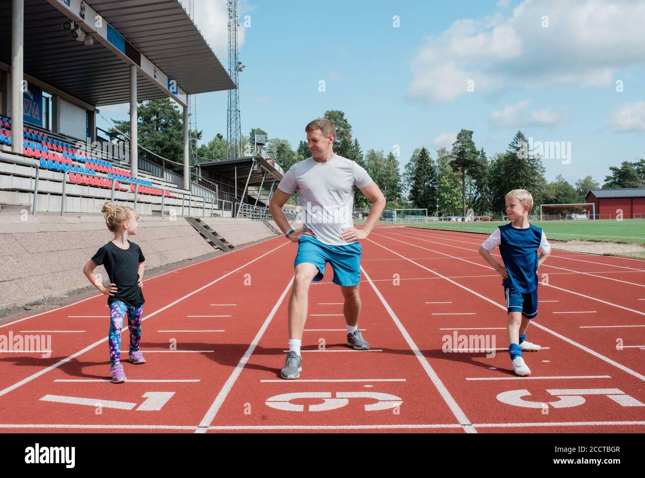 father doing stretches with his kids on a race track Stock Photo - Alamy