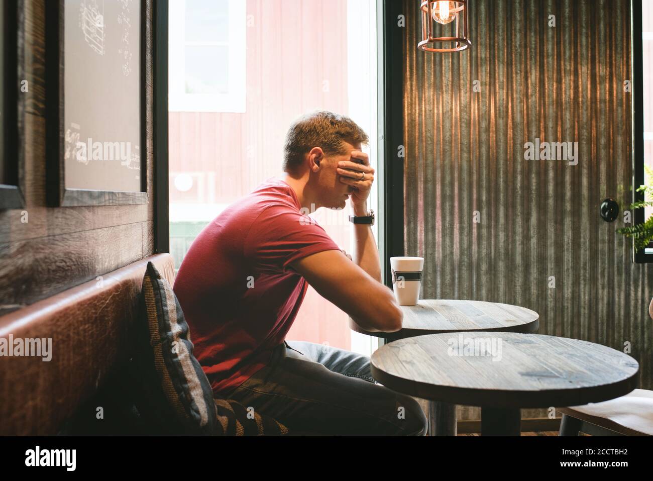 man sat covering his face feeling stressed whilst sat in a cafe Stock ...