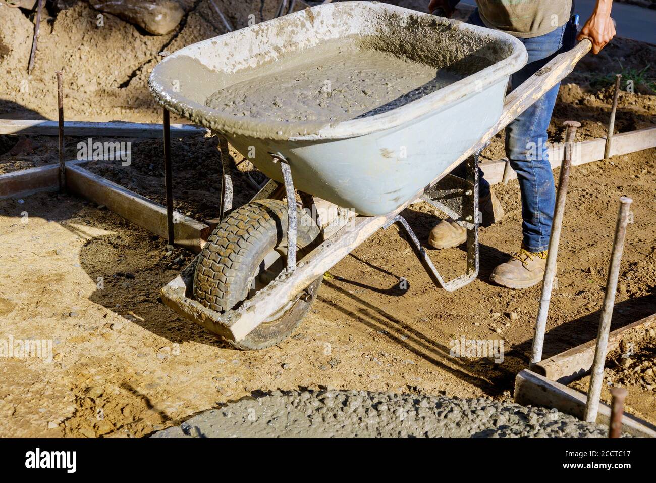 Construction worker pushing wheelbarrow with concrete at building a ...