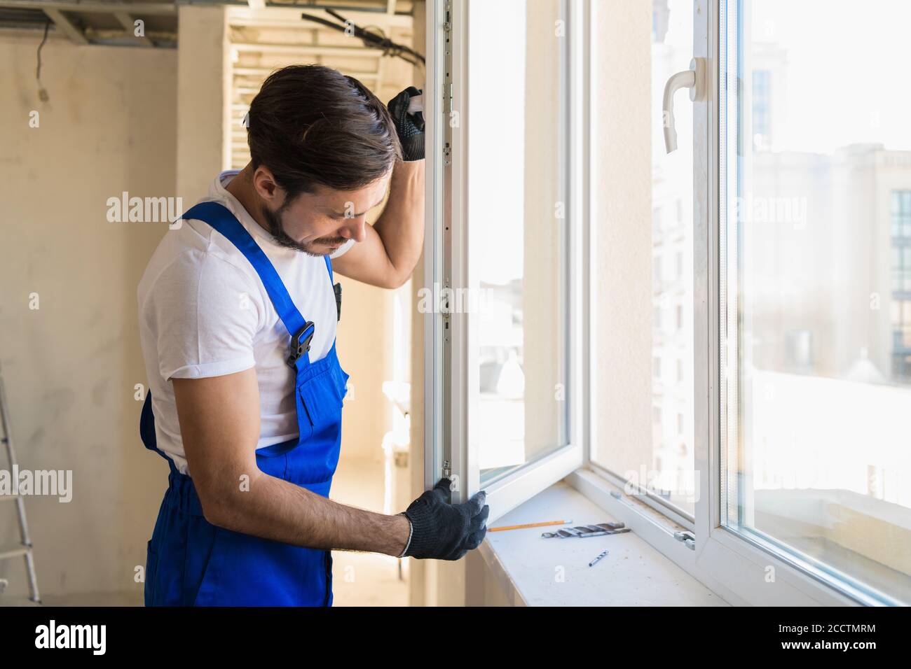 Workman in overalls and gloves checks the window frame Stock Photo - Alamy