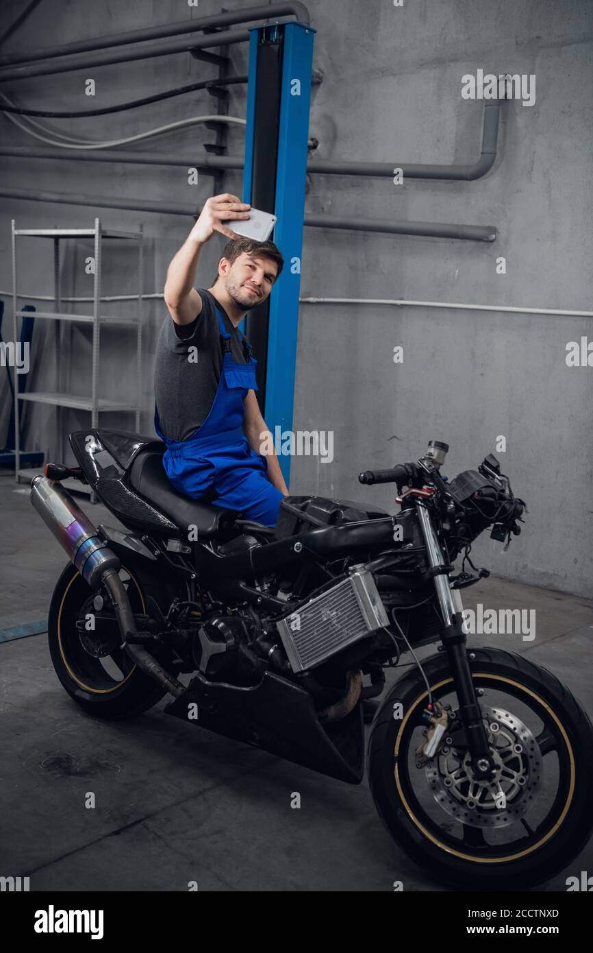 Workman in overalls sitting on a bike. He takes picture on a smartphone ...