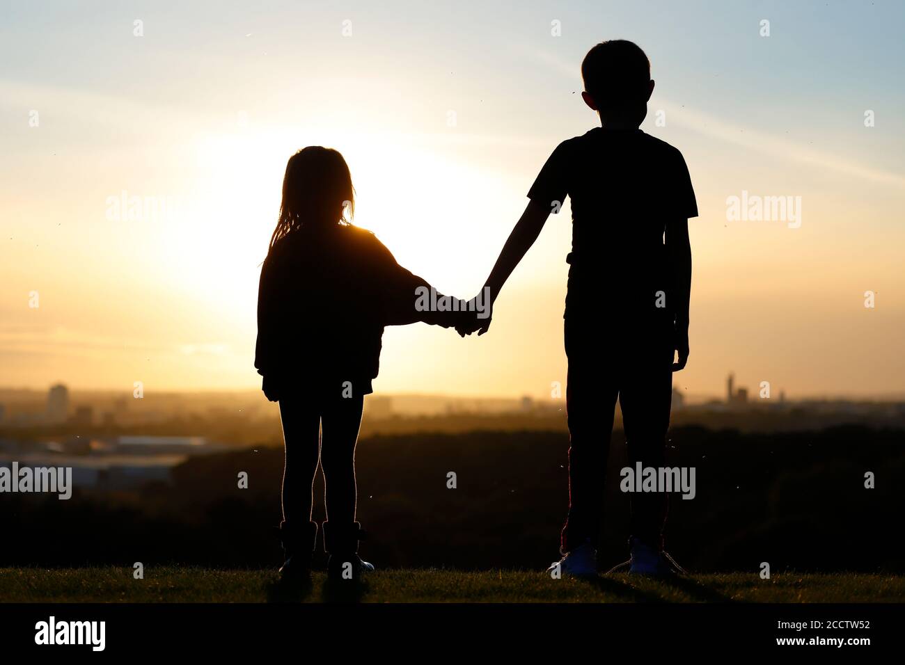 Silhouette of 2 young siblings watching the sun setting over Leeds ...