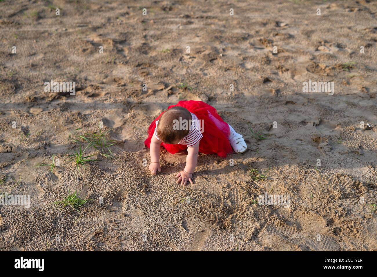 little girl in red dress is playing in sand, baby crawling on ground ...