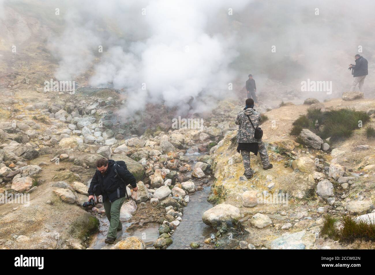 Group of travelers and photographer walks through volcanic landscape ...