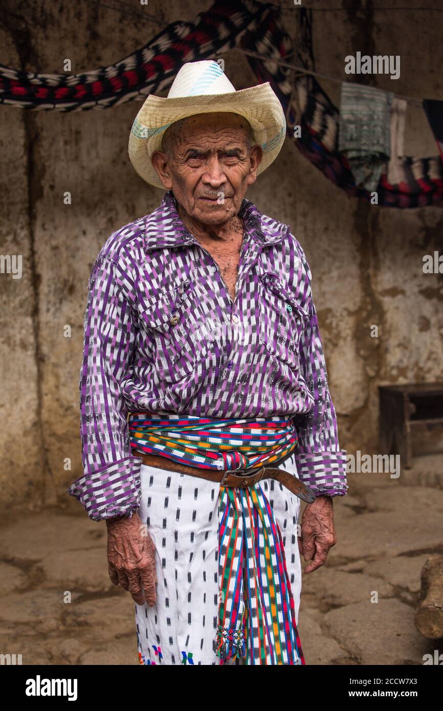 90 year old Mayan man in traditional dress stands in front of his home ...