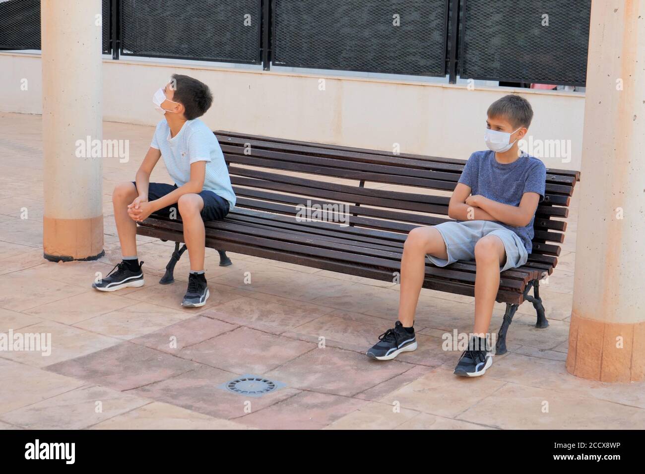 Children with medical protective masks sitting on the bench outdoors ...