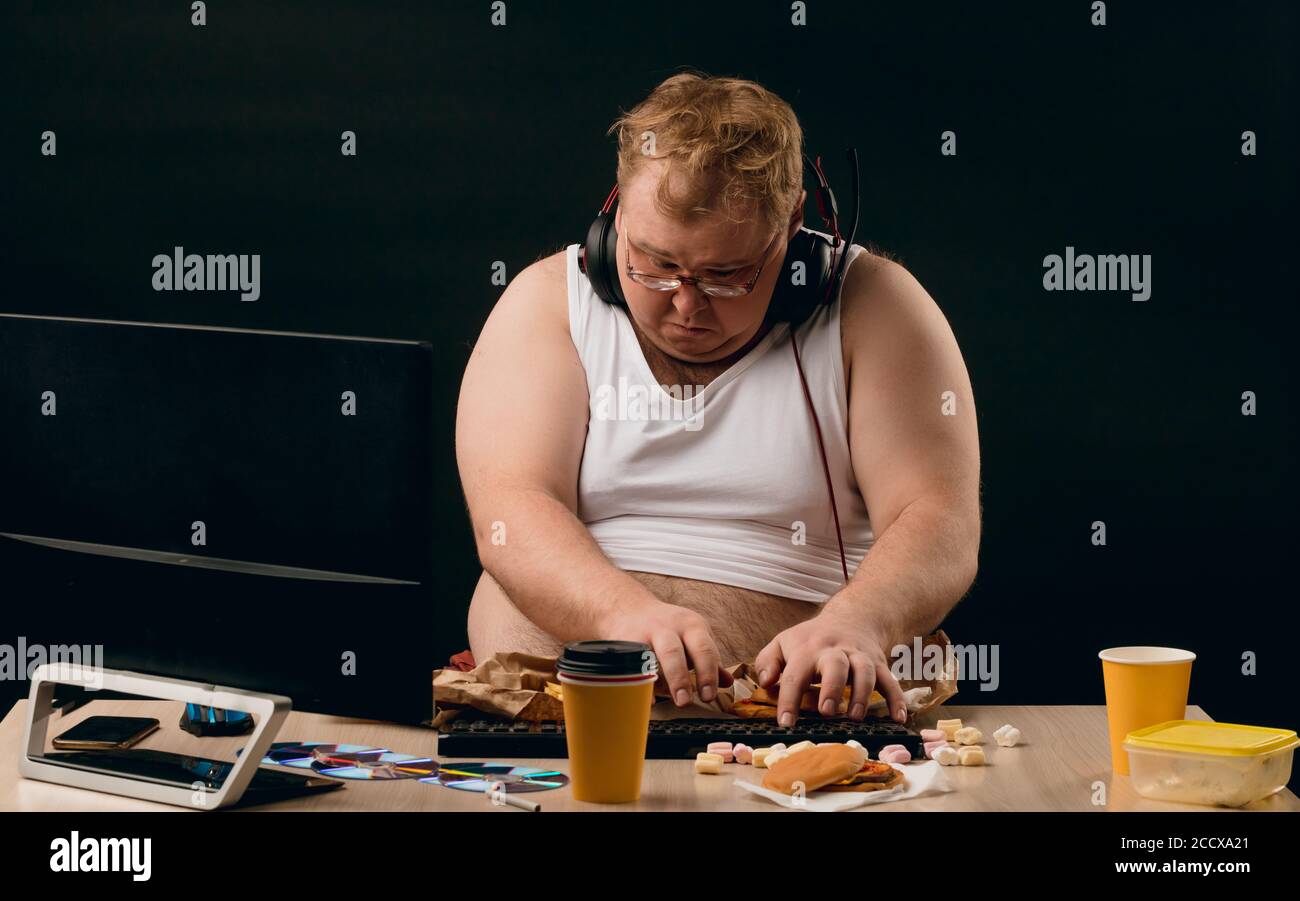Young obese man in casual clothes sitting at the table and and typing ...