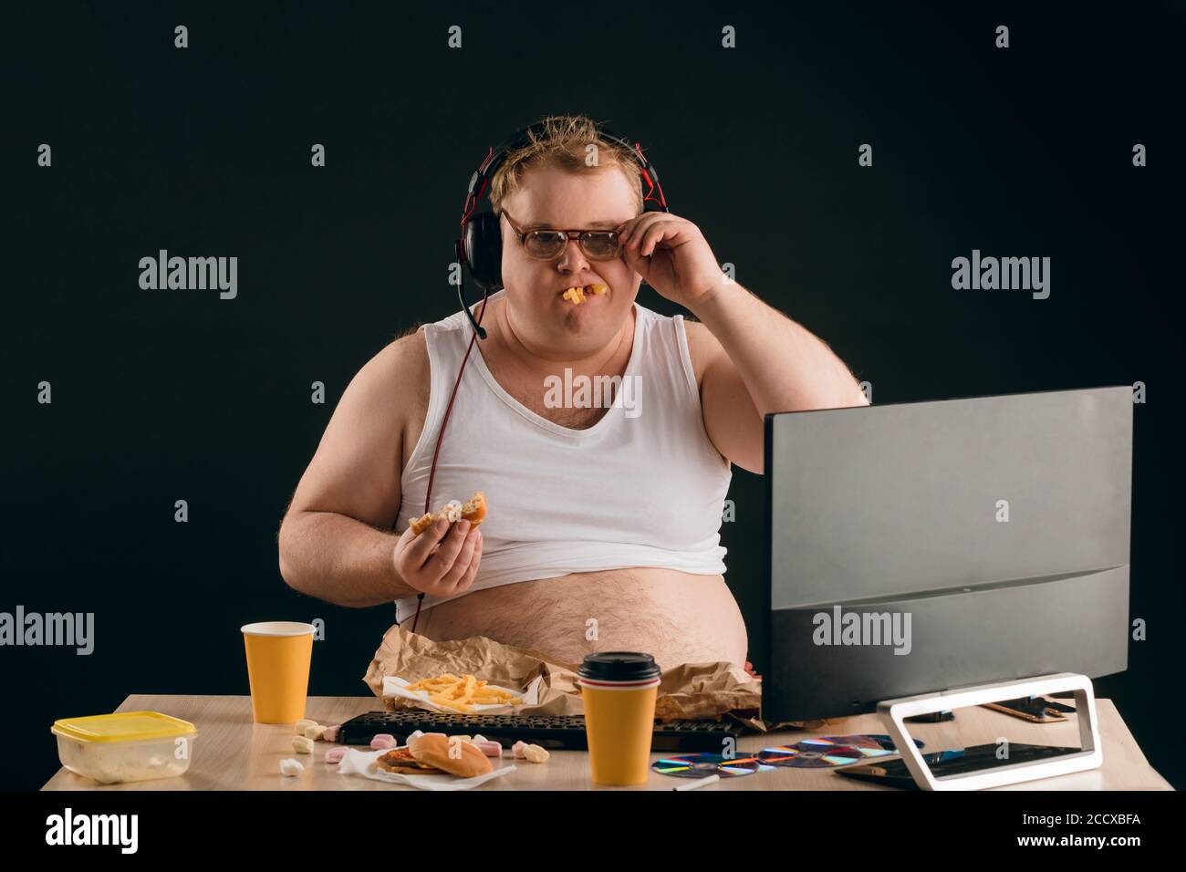 plump man with neglected look eating fried potatoes and looking at the ...