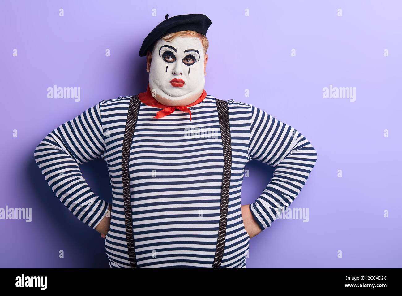 serious plump mime with white face, looking aside, holding his hands on ...