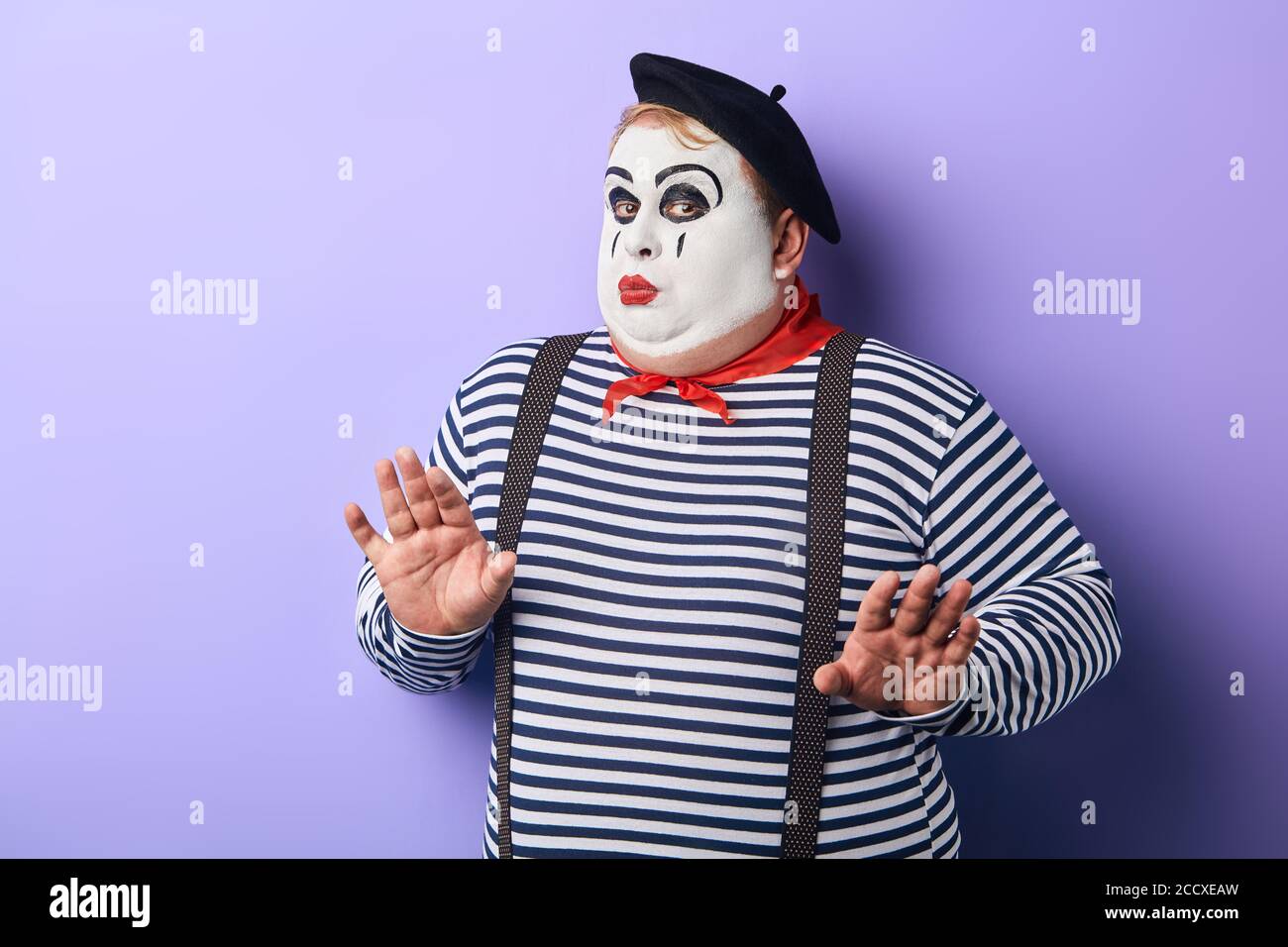 funny plump mime in stiped clothes asking not to worry, scared clown ...
