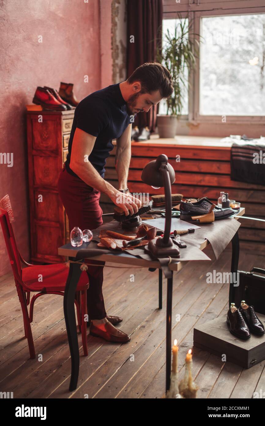young awesome man cleaning the shoes in the room with red wall, full ...