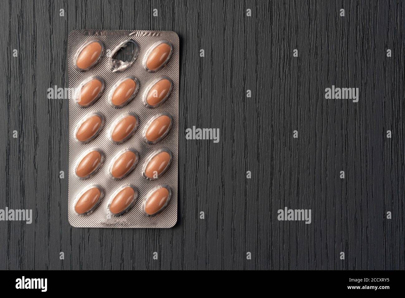 Brown pills in a silver blister pack on a dark wooden gray texture ...