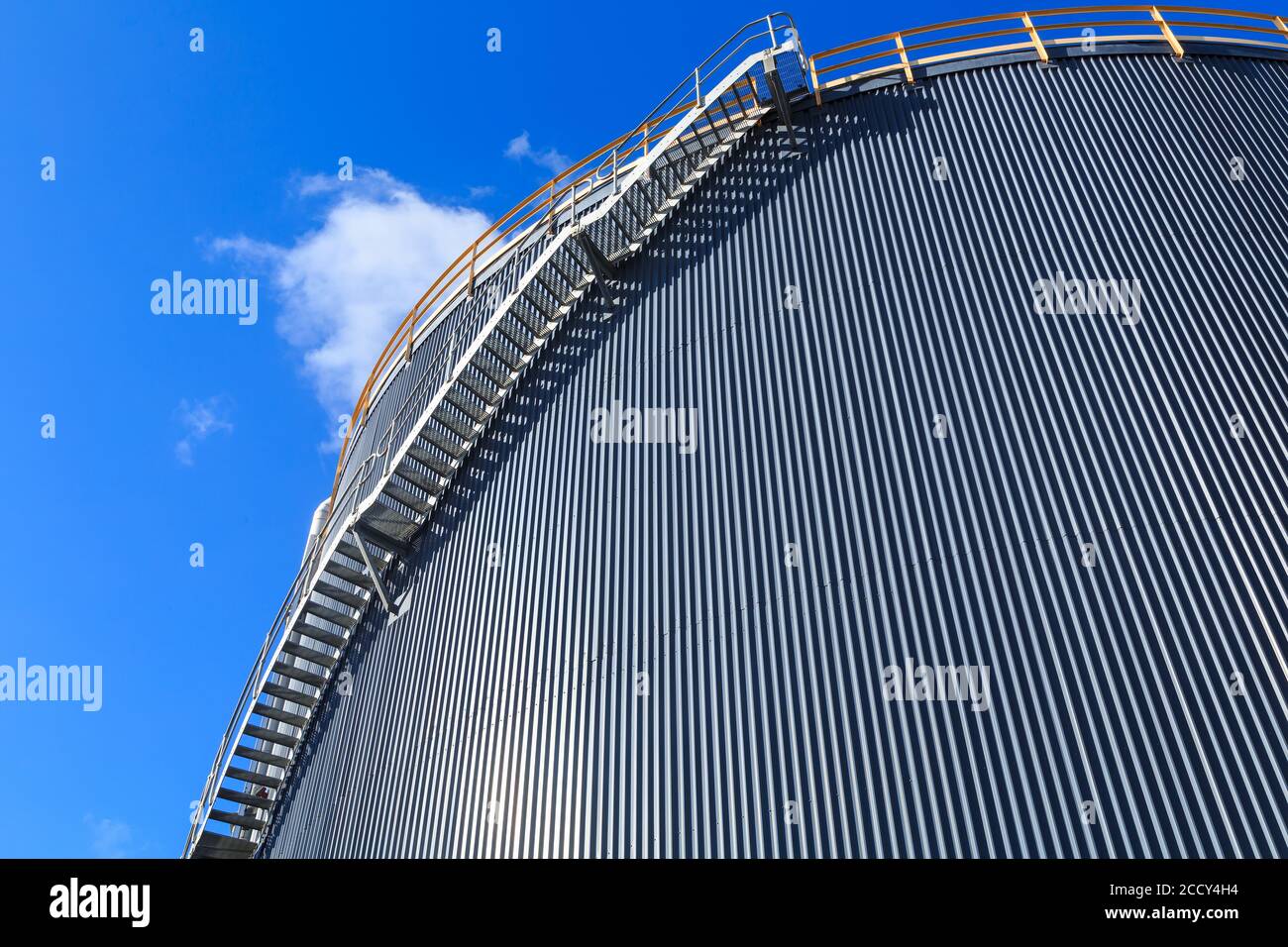The side of a huge grey storage tank, with an access stairway going to ...
